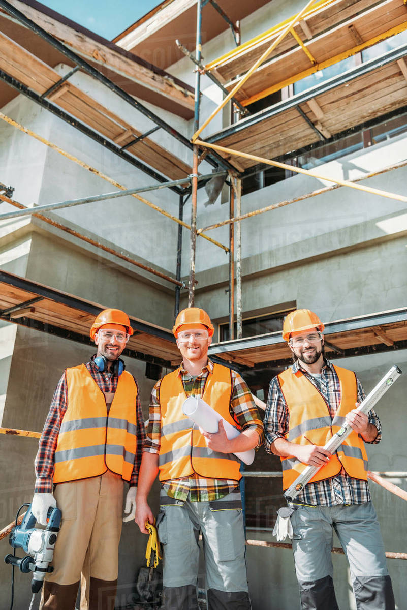 Group of smiling equipped builders looking at camera at construction ...