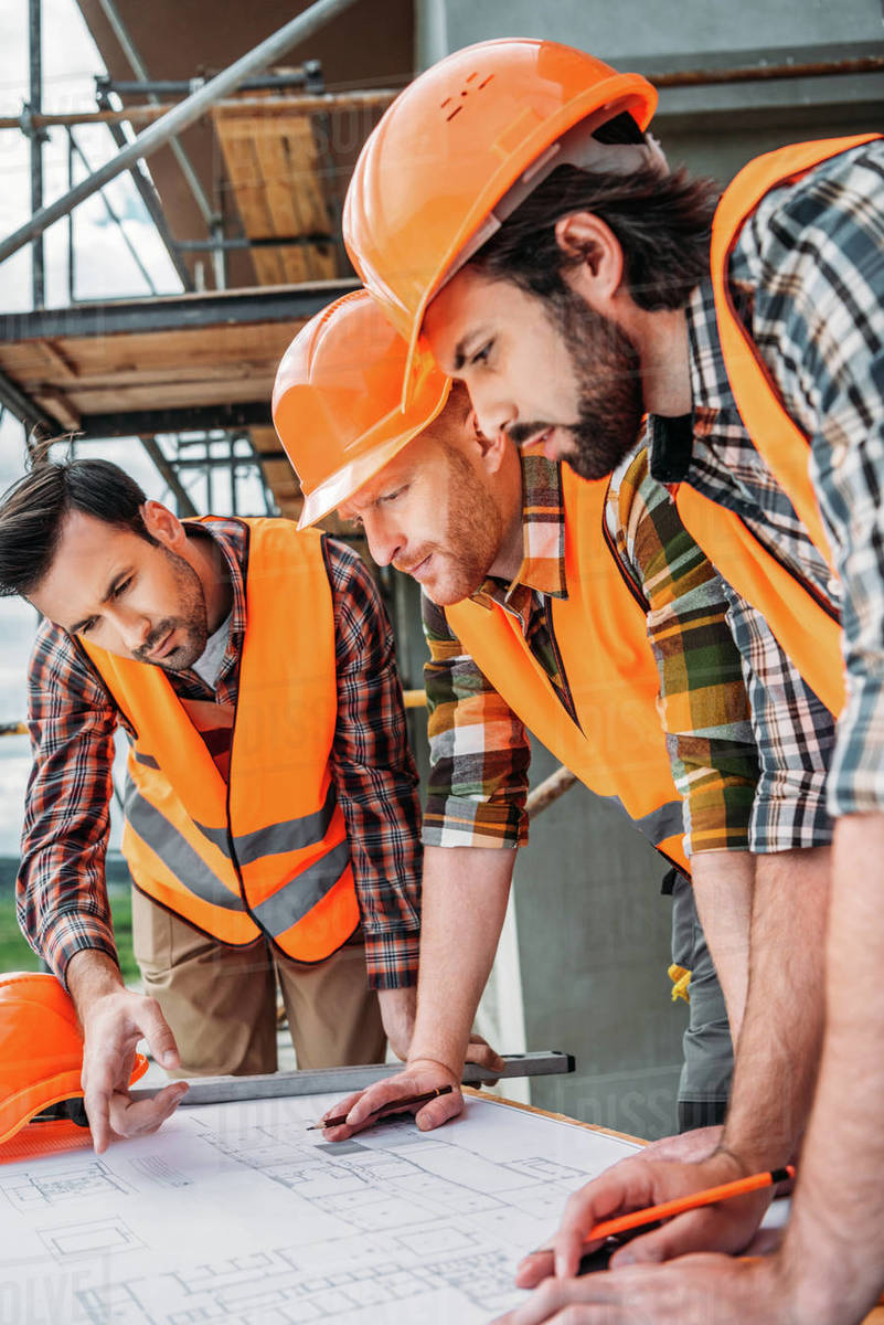 Group of serious builders looking at building plan at construction site ...