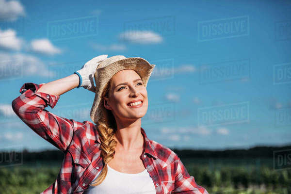 beautiful smiling young female farmer looking away while working on ...