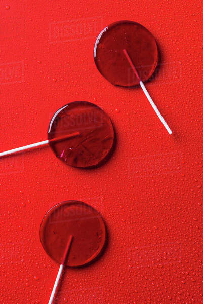 top view of three lollipops on red surface with water drops - Royalty ...