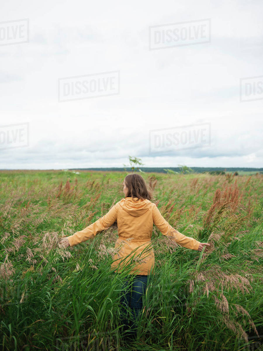 Young woman in yellow jacket with raised arms standing in field against ...
