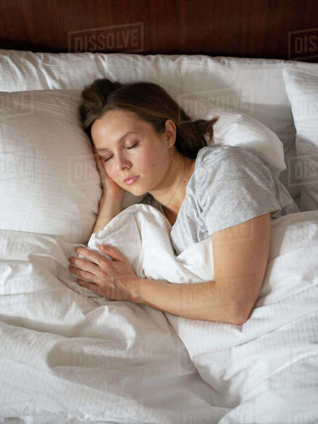 Woman sleeping in bed putting her hand under head - Stock Photo - Dissolve