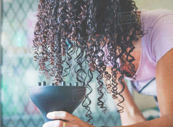 Close-Up of a woman bending over and drying her curly hair with a hair ...