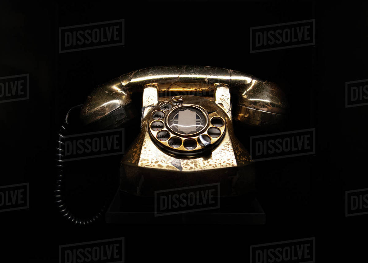 Close-up of an old fashioned gold phone against a black background ...