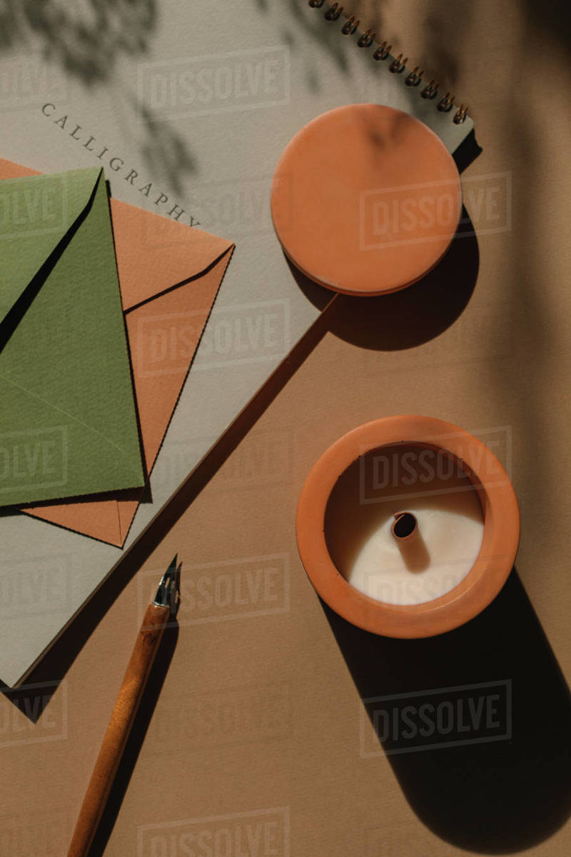 Overhead view of a candle, calligraphy pen, envelopes and a calligraphy ...