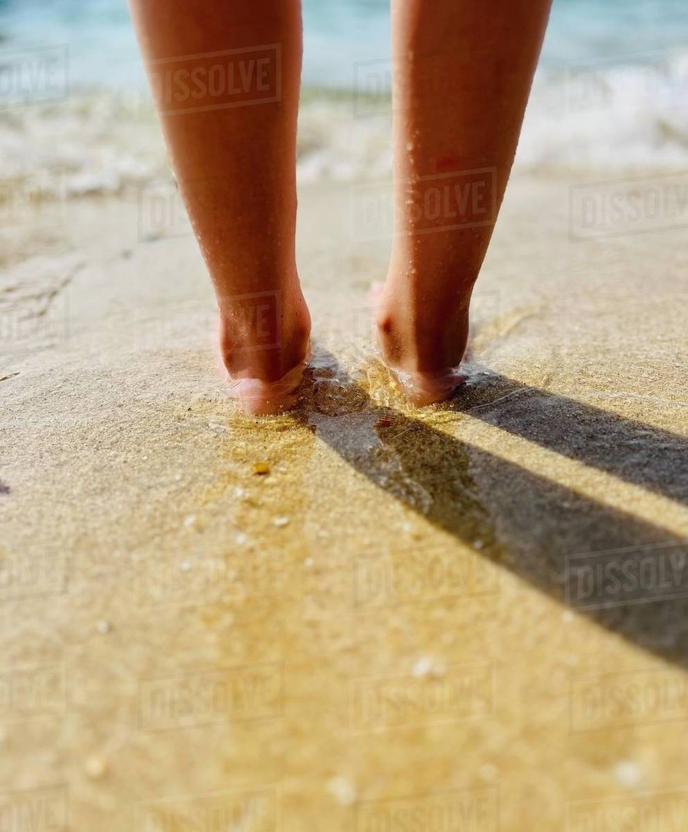 Close-up rear view of a person standing ankle deep in Aegean Sea ...
