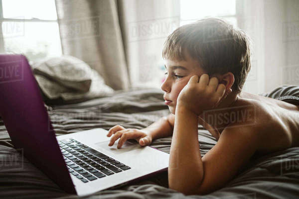Shirtless boy lying on his bed using a laptop computer - Royalty-free ...