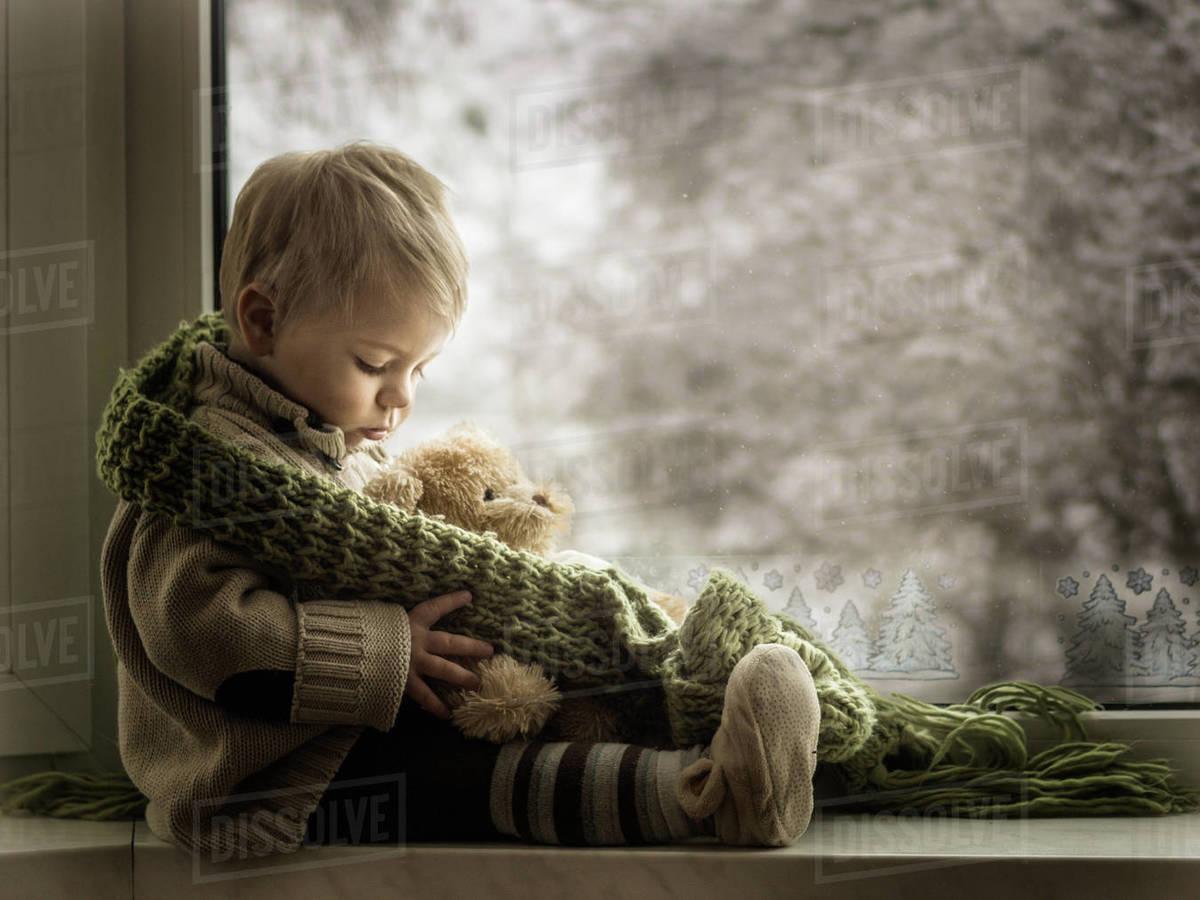 Boy sitting on a window sill with a teddy bear - Stock Photo - Dissolve