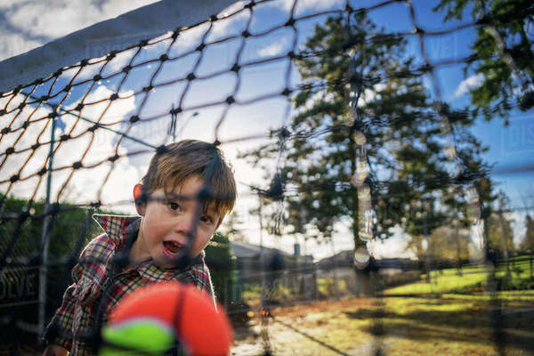 View through a net of a boy throwing tennis ball - Stock Photo - Dissolve