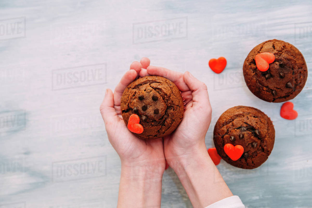 Girl's hands holding chocolate muffins with hearts - Stock Photo - Dissolve