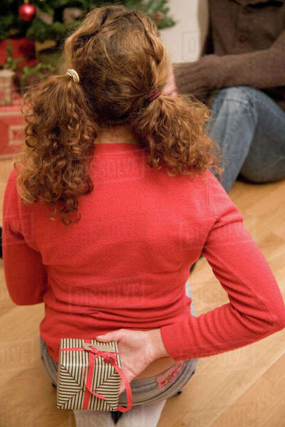 Little girl hiding gift behind her back - Stock Photo - Dissolve