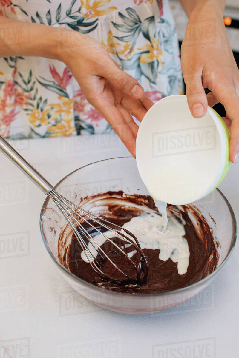 Woman adding milk to chocolate cake mixture - Stock Photo - Dissolve