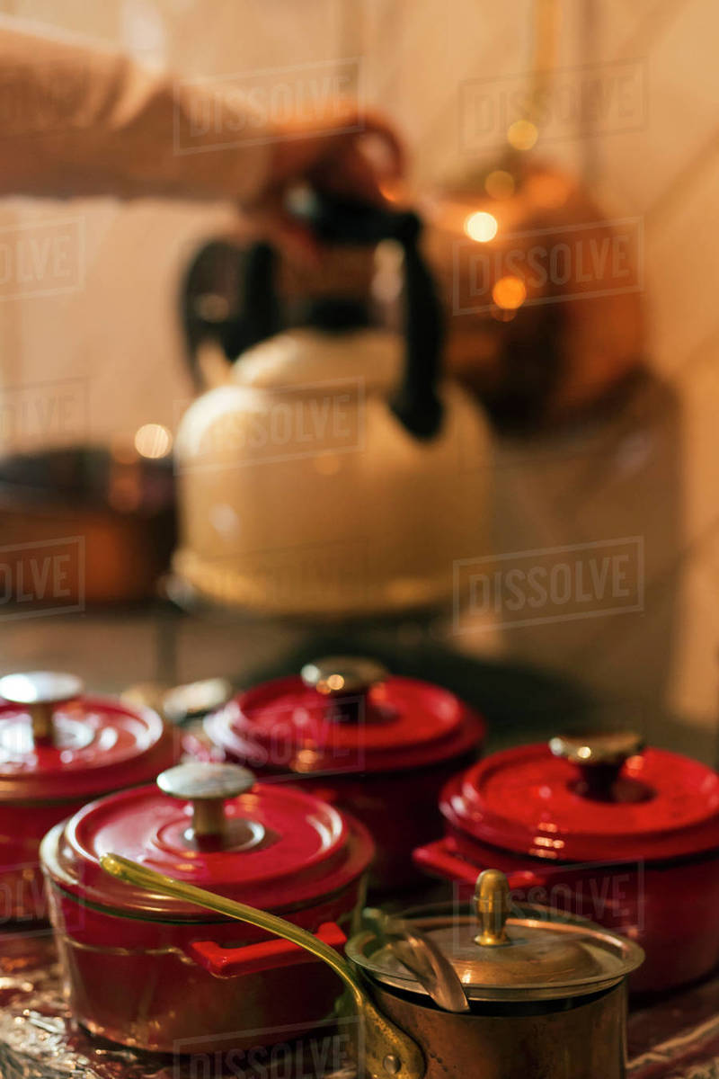 Human hand putting a kettle on a kitchen worktop by small casseroles ...