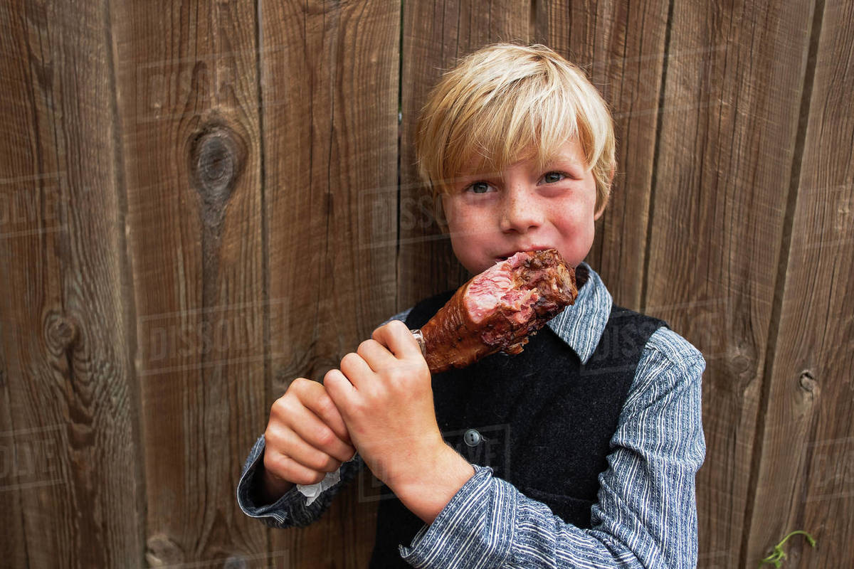 Boy standing by a fence eating a barbecued turkey leg, USA - Royalty ...