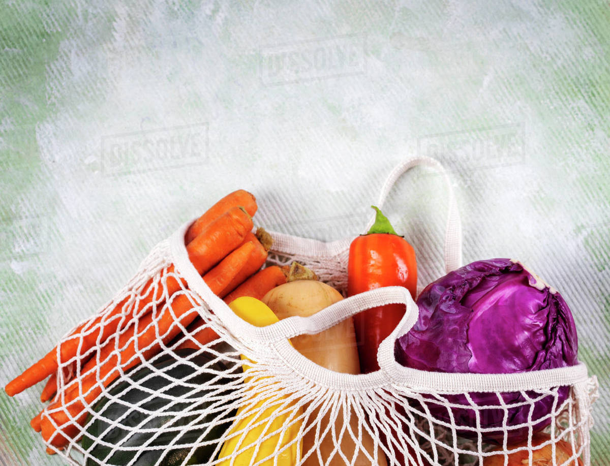 Reusable mesh bag with assorted fruit and vegetables on a table ...