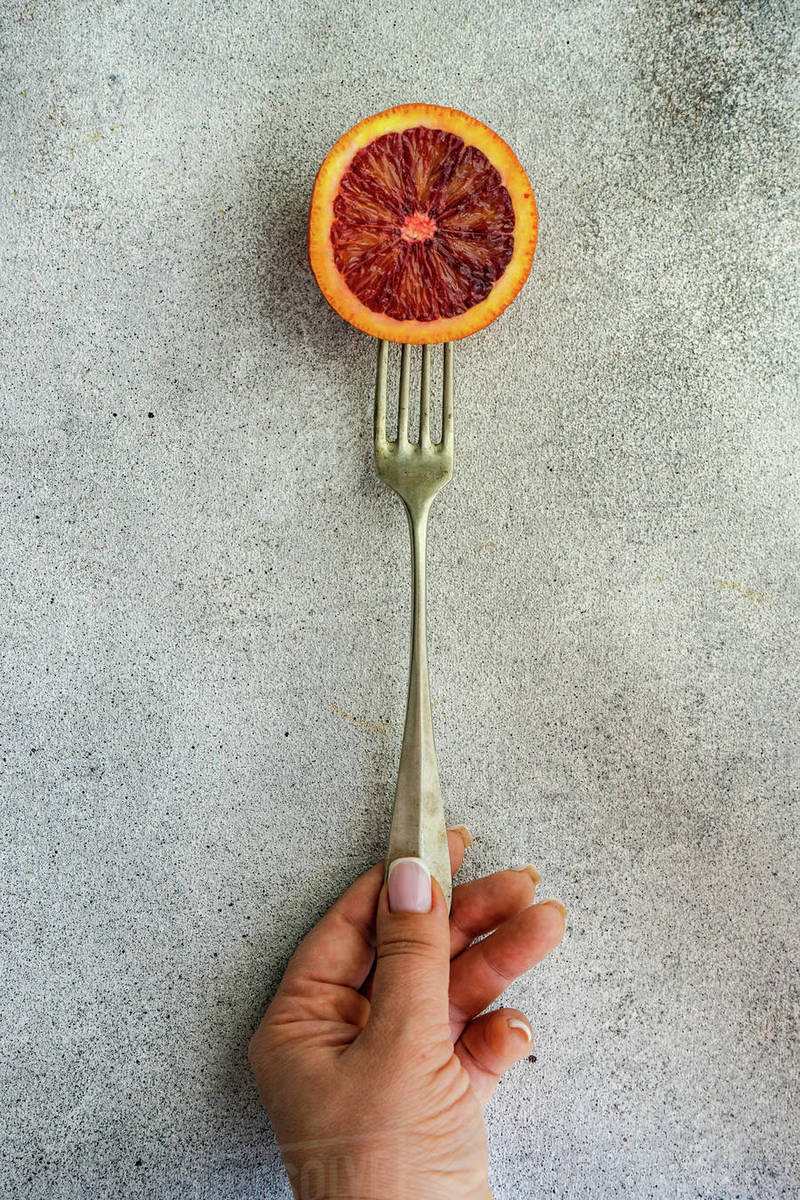 Overhead view of a hand holding a fork with half a Sicilian blood ...