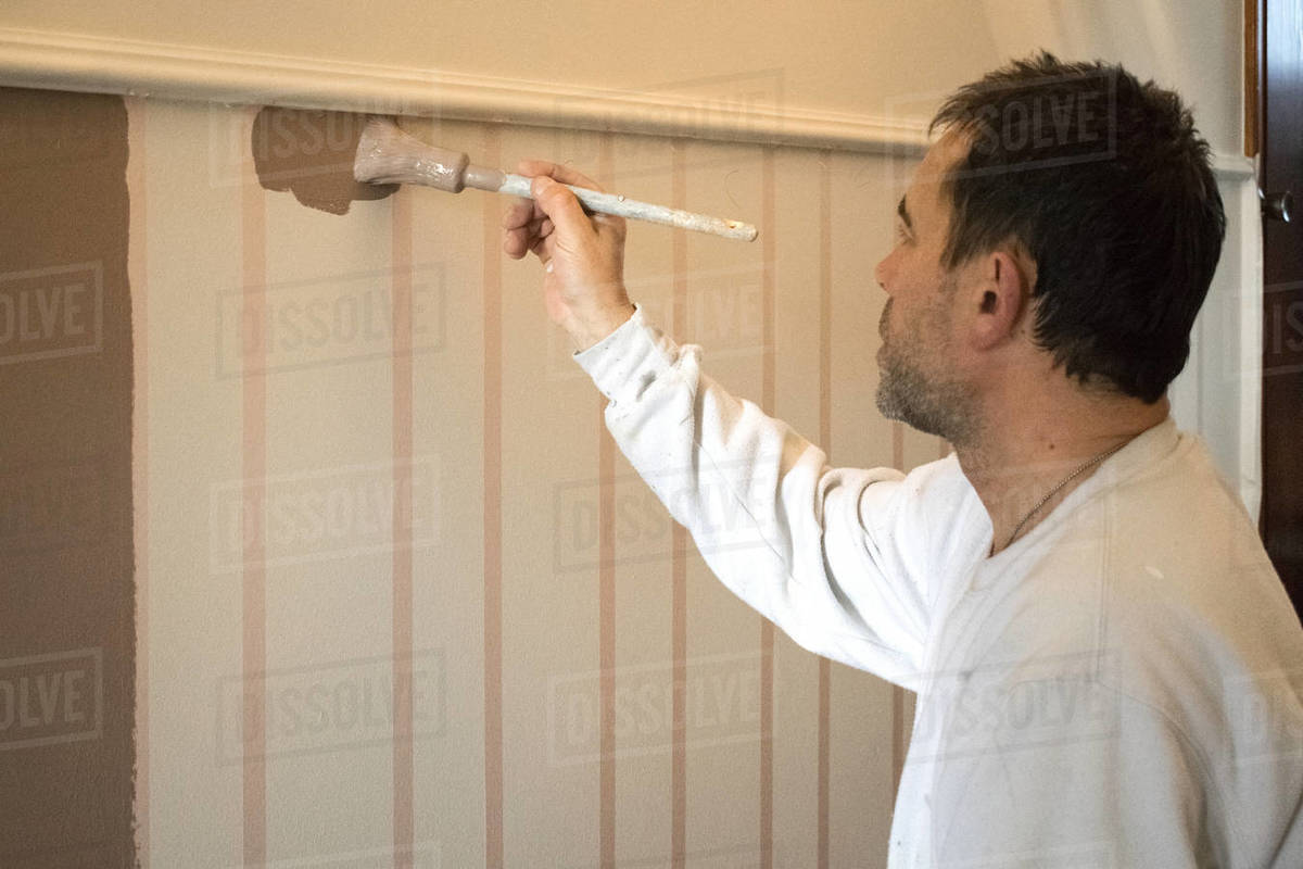 Painter painting stripes on a wall below a dado rail with a paint brush ...
