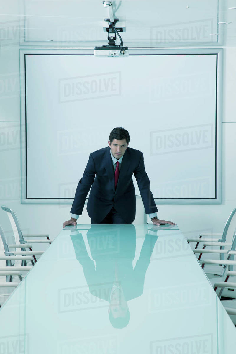 Businessman standing at the head of conference table in office ...