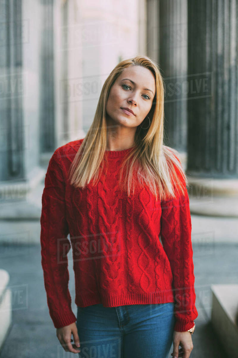 Pretty young woman in trendy red sweater looking at camera while ...