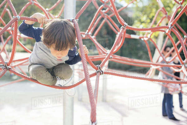Pensive relaxed kid hanging on rope climbing net on playground in ...