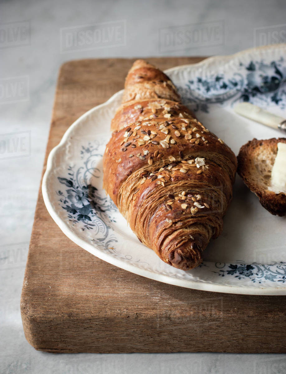Closeup of golden crunchy croissant with grains served on plate on ...
