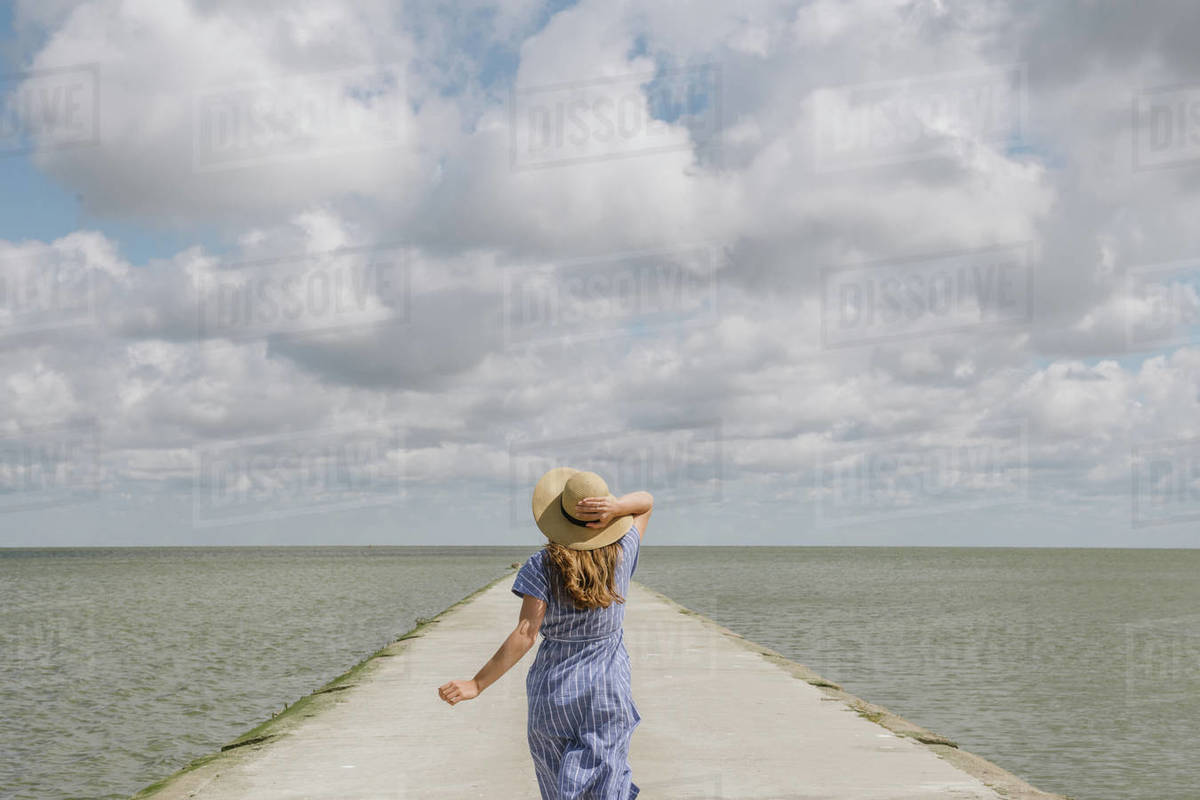 Back view of adult woman in straw hat and sundress running on empty ...
