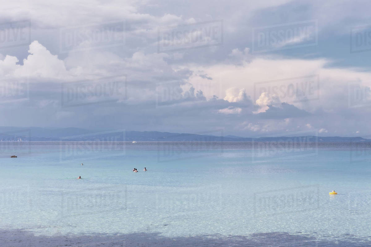 Peaceful sea water with people swimming in calm weather under cloudy ...