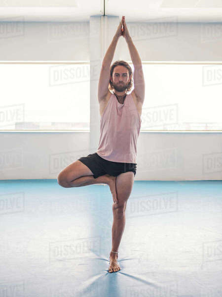 Bearded man in sportswear standing in one leg with prayer hands looking ...