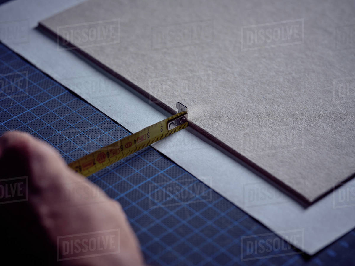 Hand of craftsman using steel ruler to measure paper border for folding ...