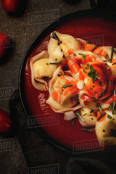 Cooked ravioli with tomato sauce and herbs in bowl next to fork and ...