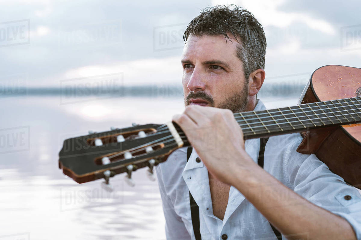 Wistful man in white shirt and suspenders carrying acoustic guitar and ...
