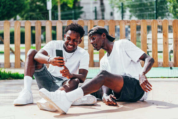 Cheerful amusing African American sportsmen surfing mobile phone ...