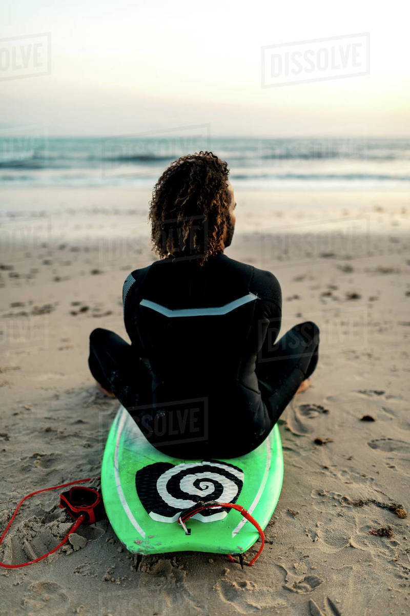 Full body back view of male surfer with fluffy hair in black wetsuit ...