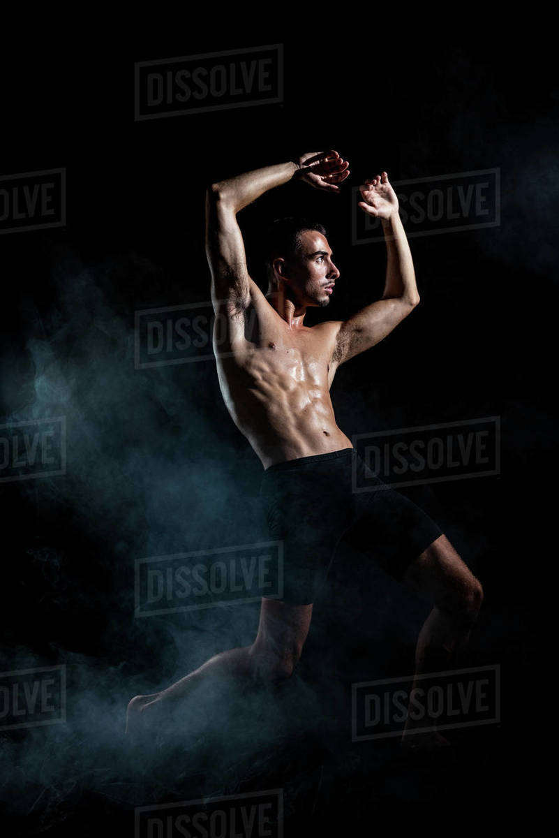 Full body of faceless tanned sporty shirtless dancer in shorts raising ...