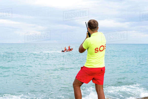 Back view unrecognizable lifeguard in bright uniform whistling and ...