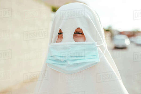 Anonymous spooky person wearing white ghost costume and medical mask ...