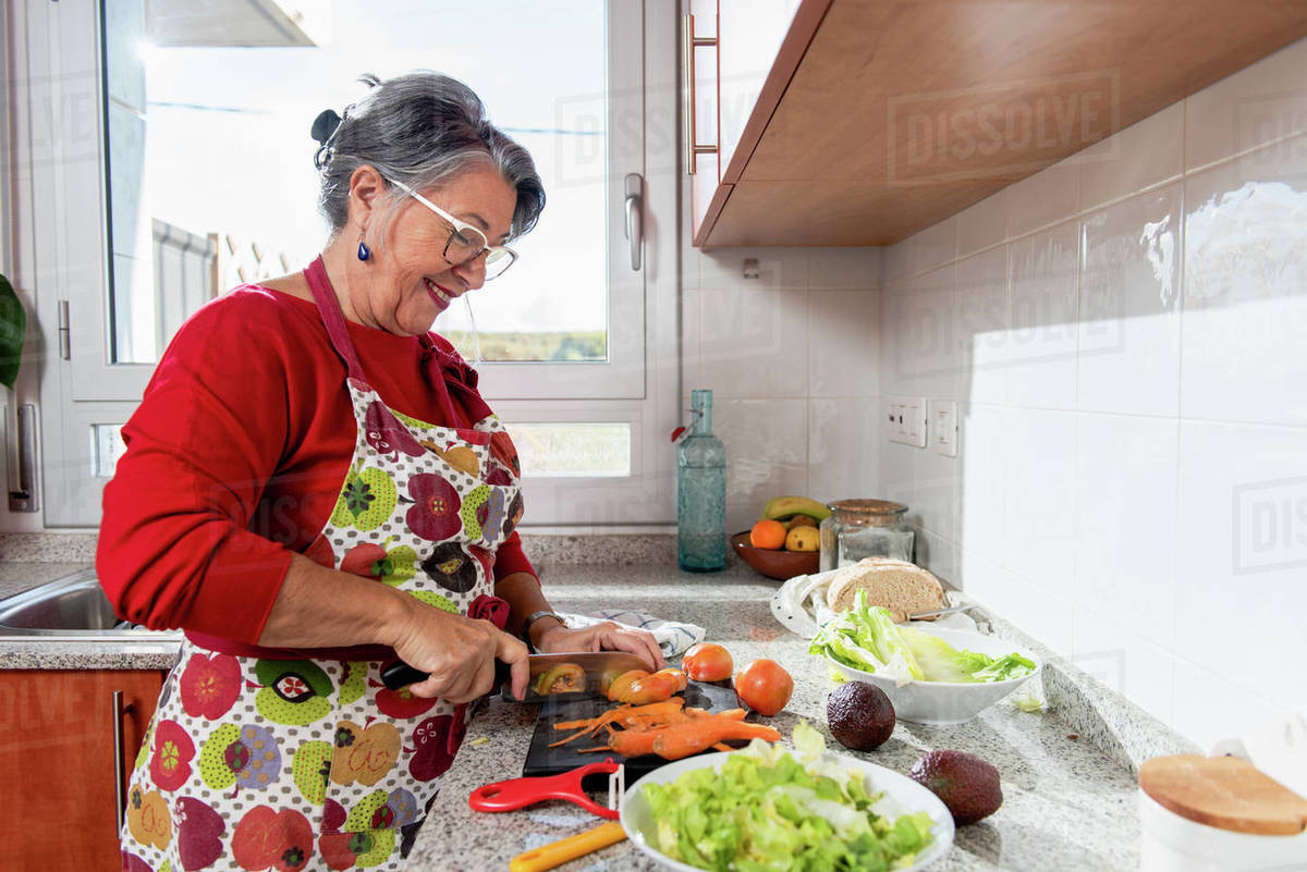 Side view content grandma in apron cutting tomatoes while cooking ...