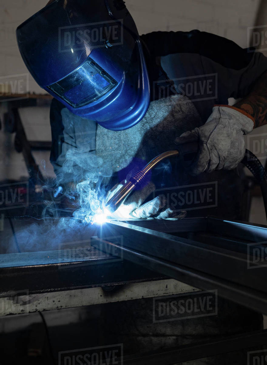 Unrecognizable male welder using welding machine on metal detail while ...