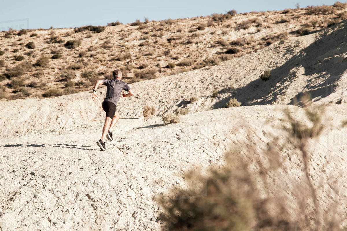 Back view of unrecognizable active male jogger running uphill in sandy ...