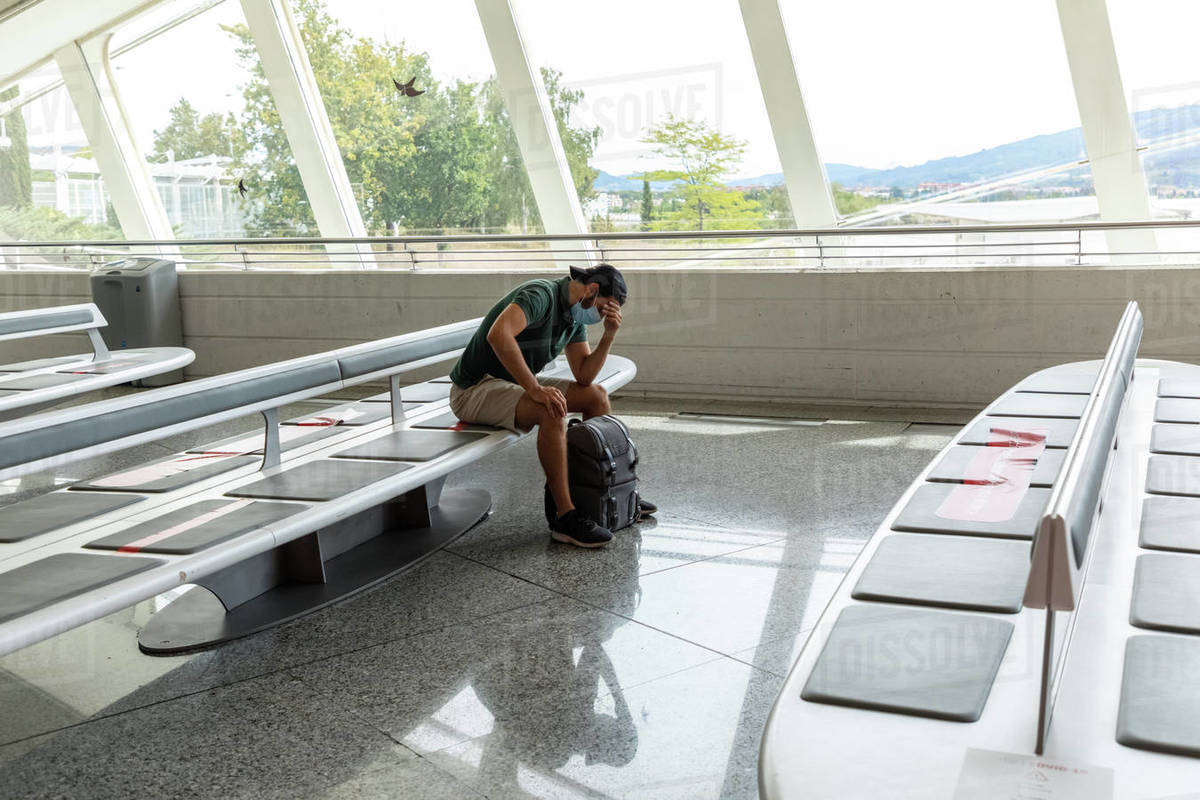 Side view of discouraged male tourist in protective mask sitting in ...