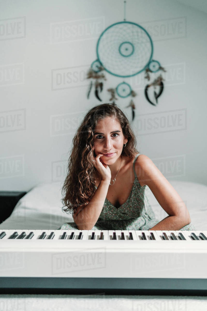 Calm ethnic female musician sitting on bed with contemporary electric ...