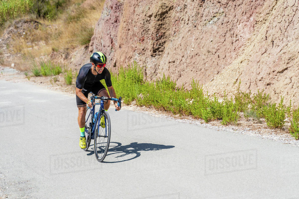 Full length of strong male bicyclist riding bike on curvy paved road ...