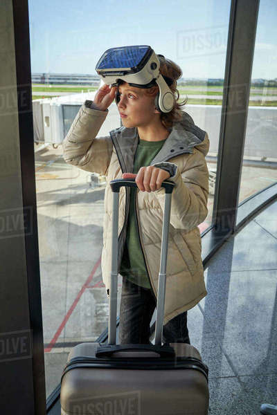 Delighted preteen passenger with VR glasses and luggage smiling and ...