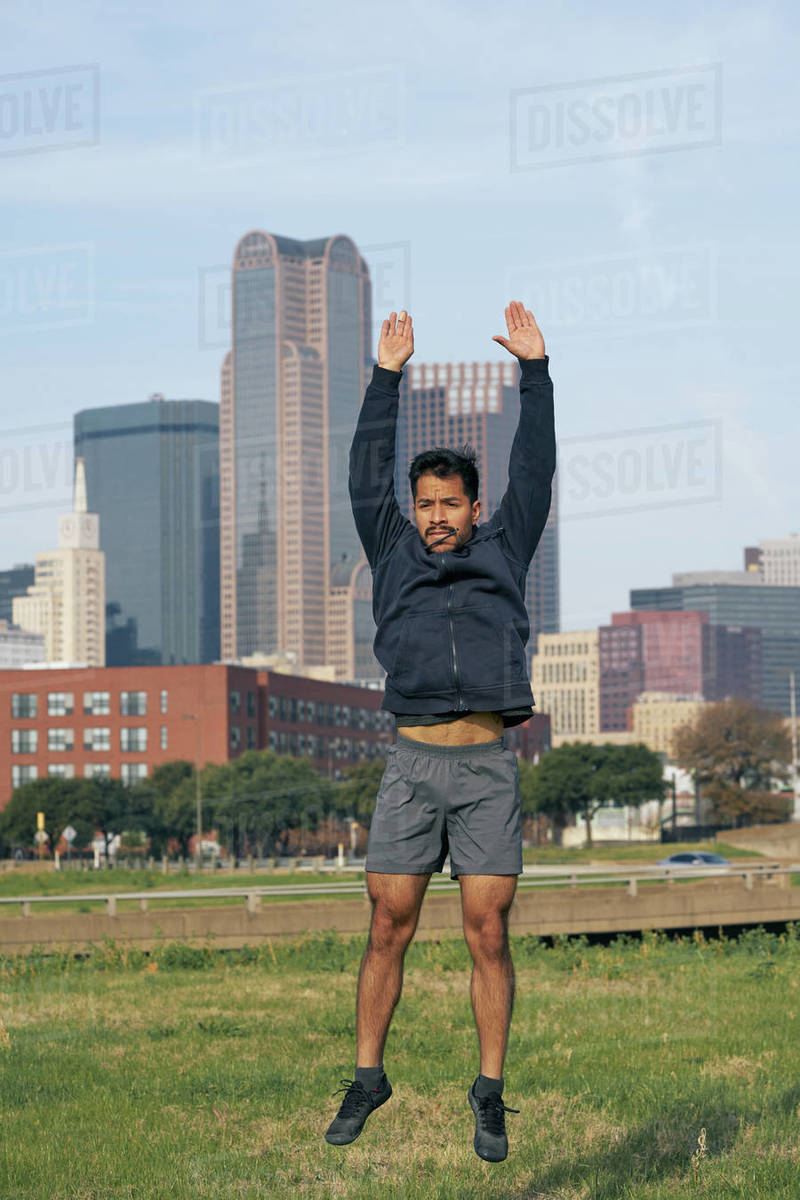 Hispanic male athlete in active wear jumping with overstretched arms ...