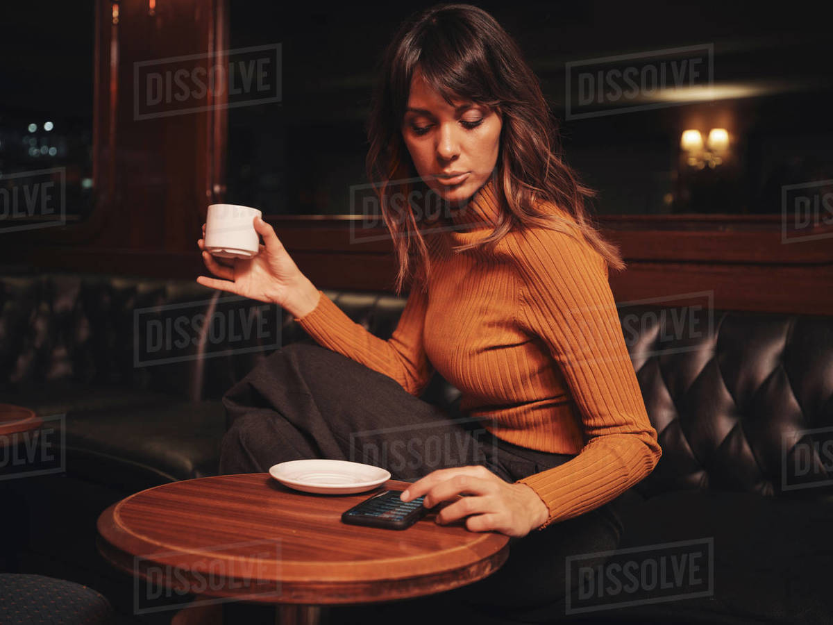 Smart woman surfing mobile phone comfortably sitting at round table and ...