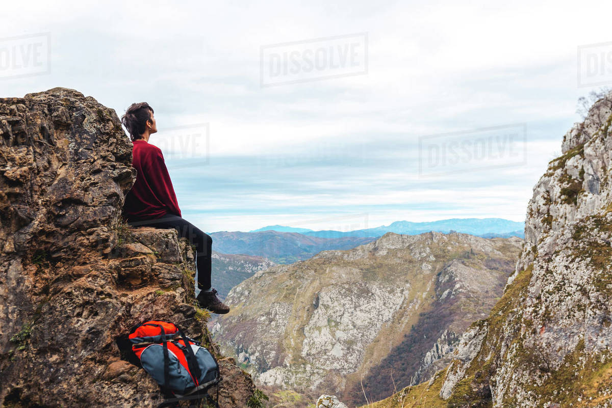 Side view of tourist sitting on edge of cliff enjoying freedom and ...