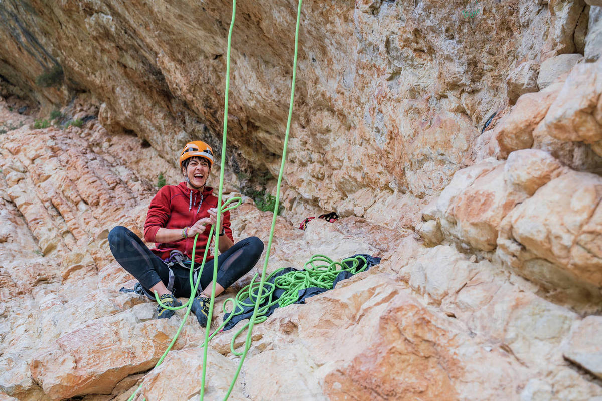 Joyful sportive female climber laughing and checking equipment while ...