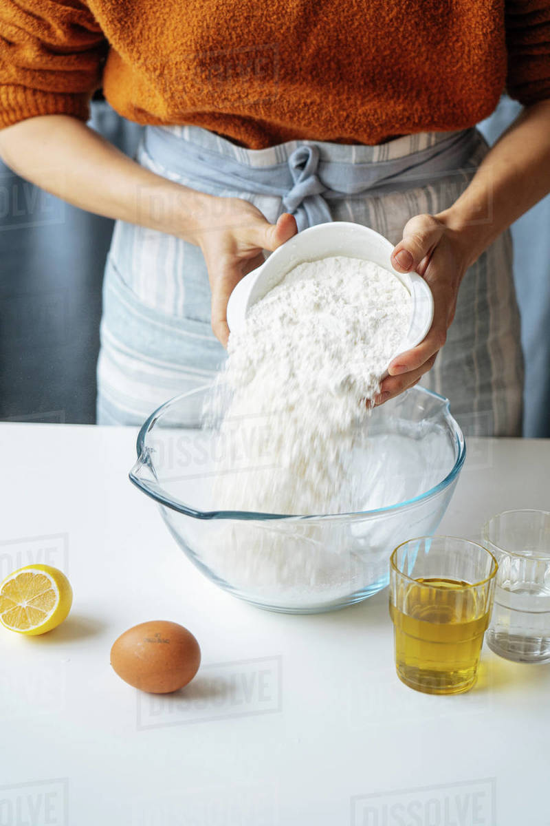 Crop housewife putting white flour into large glass bowl while ...