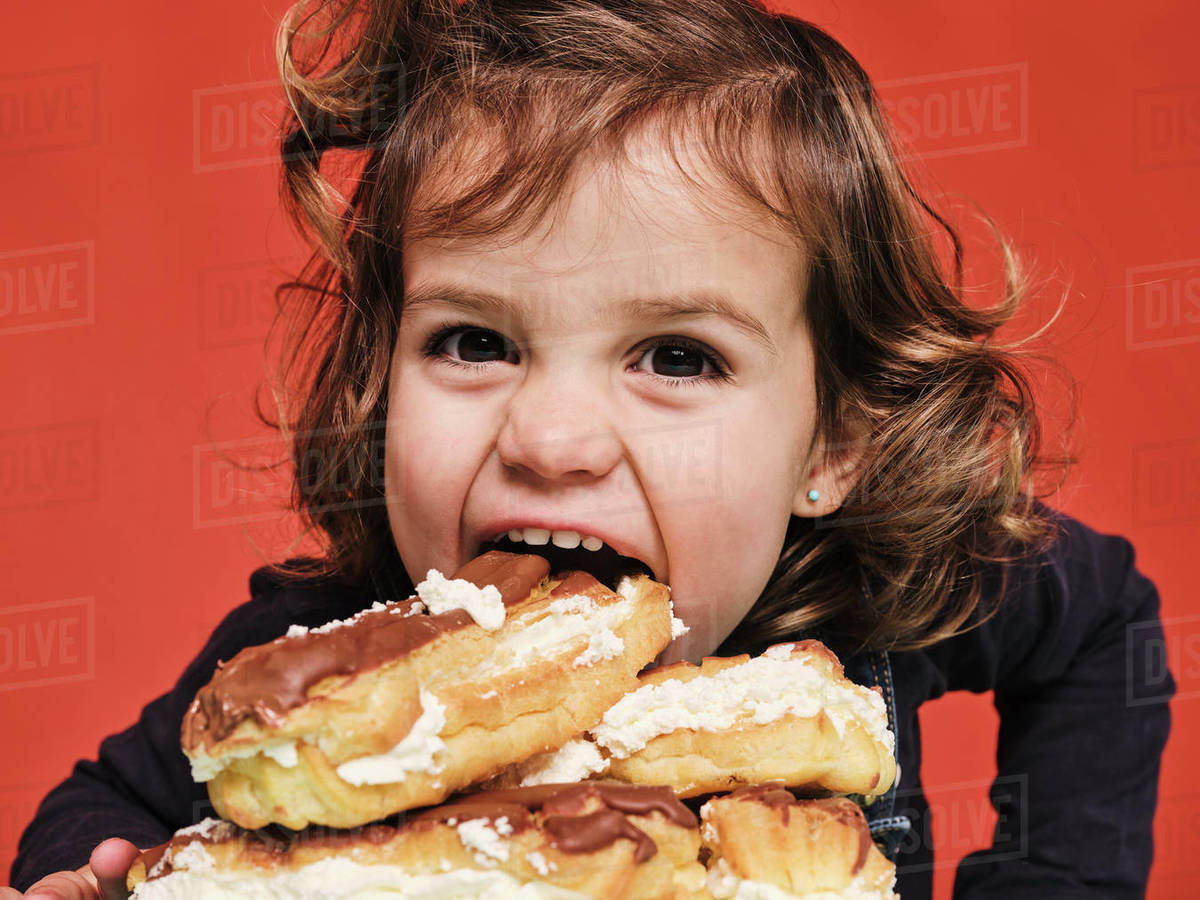 Closeup portrait of cheerful little girl enjoying sweet eclairs with ...