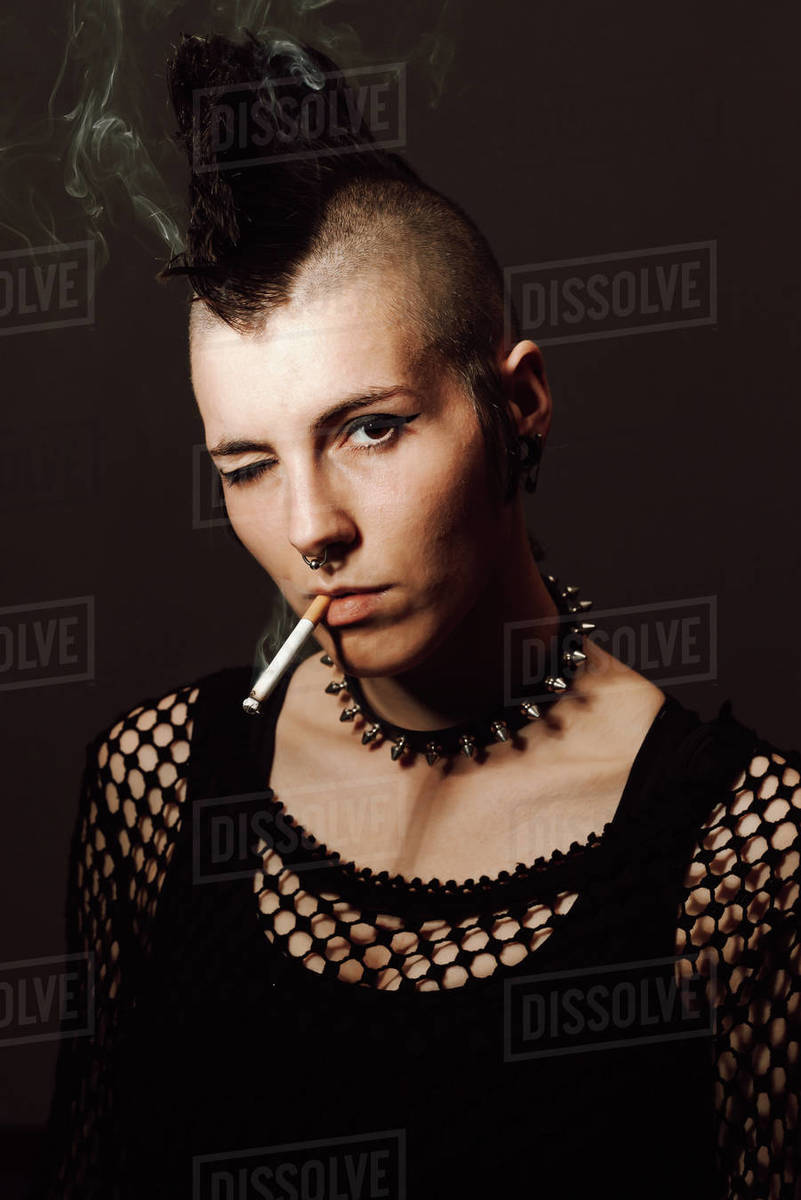 Adult female with mohawk and piercing looking at camera and igniting ...
